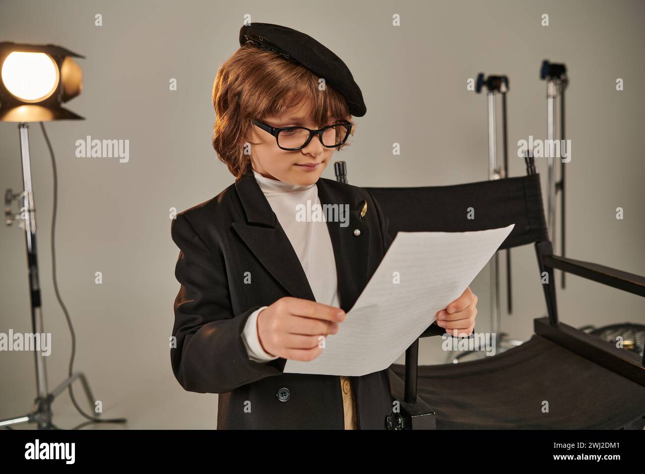 stylish kid in glasses and beret reading screenplay on papers, boy as ...