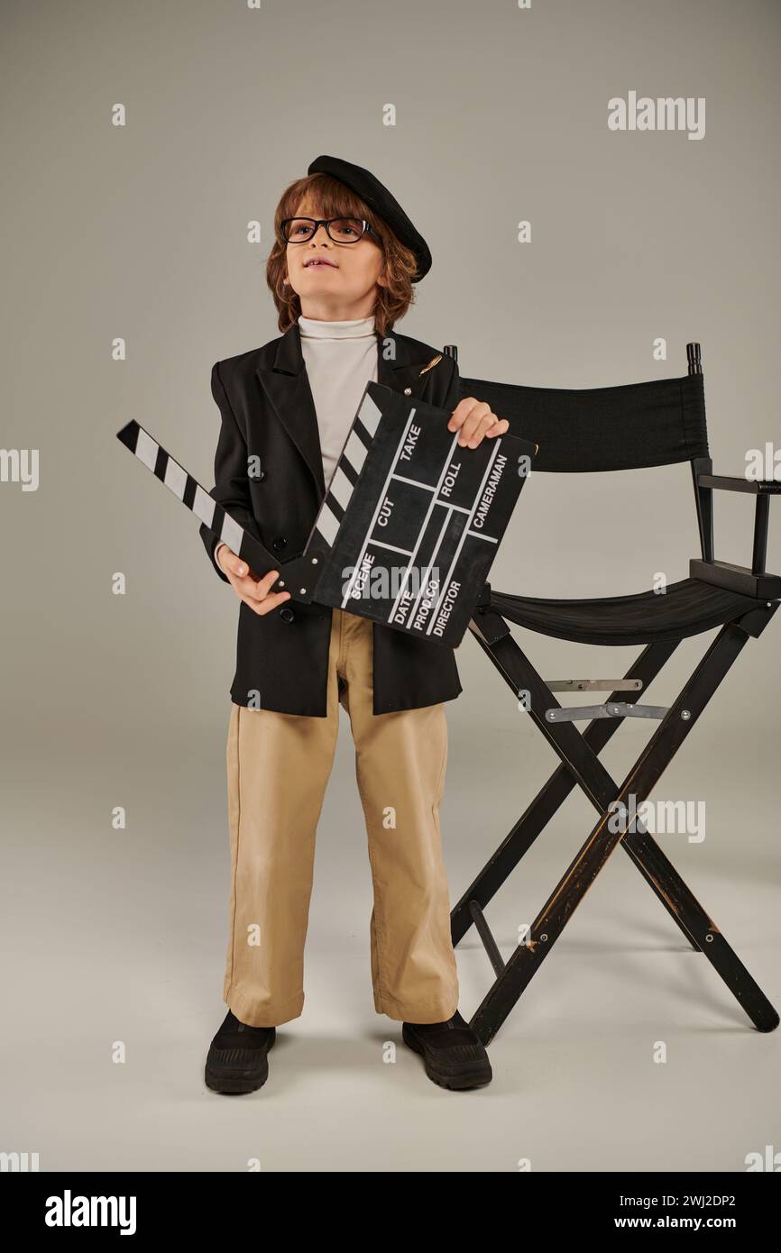stylish director boy in beret and glasses holding clapper board and ...