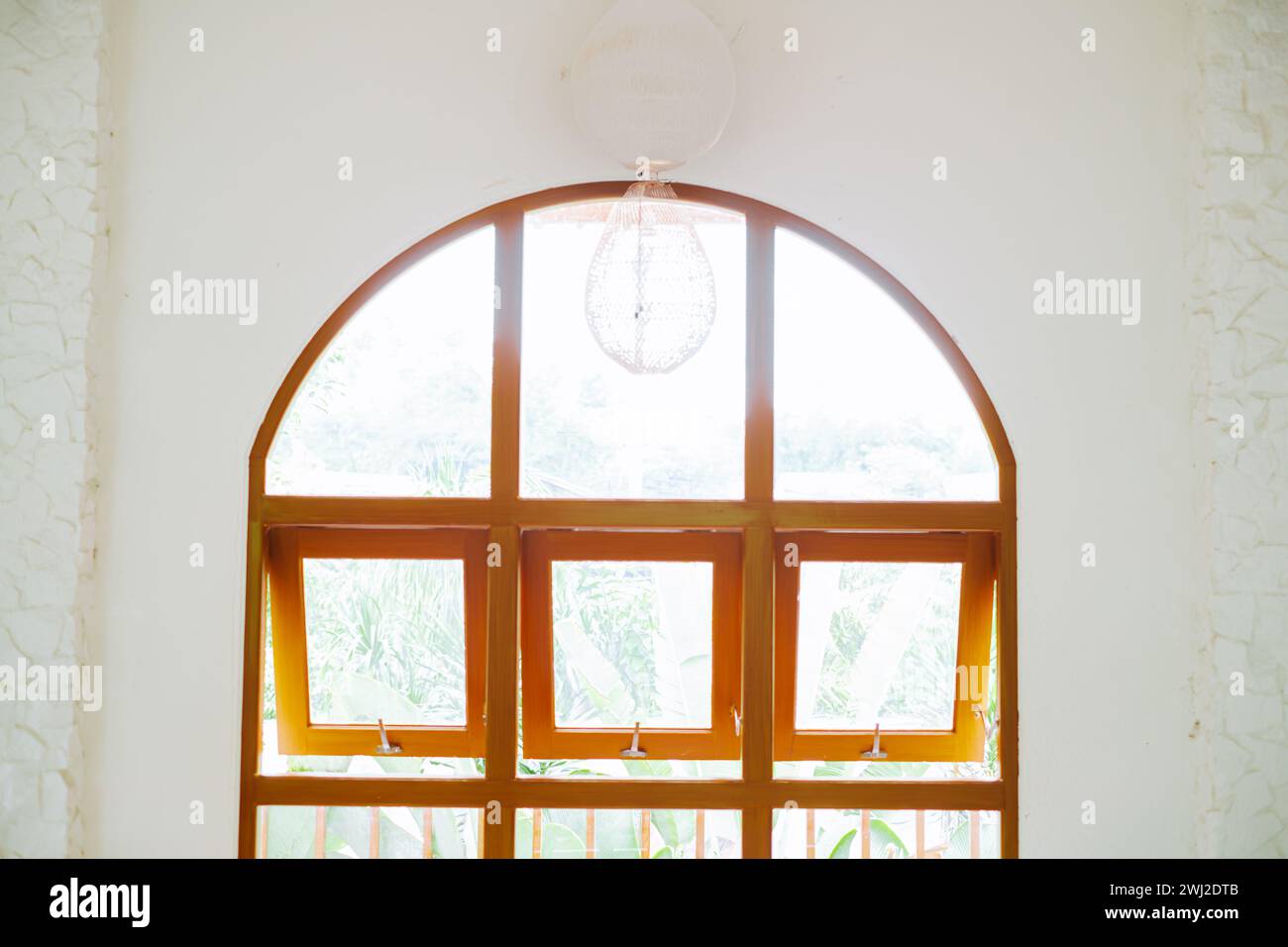 Wooden arched window against clear white wall with lush greenery ...