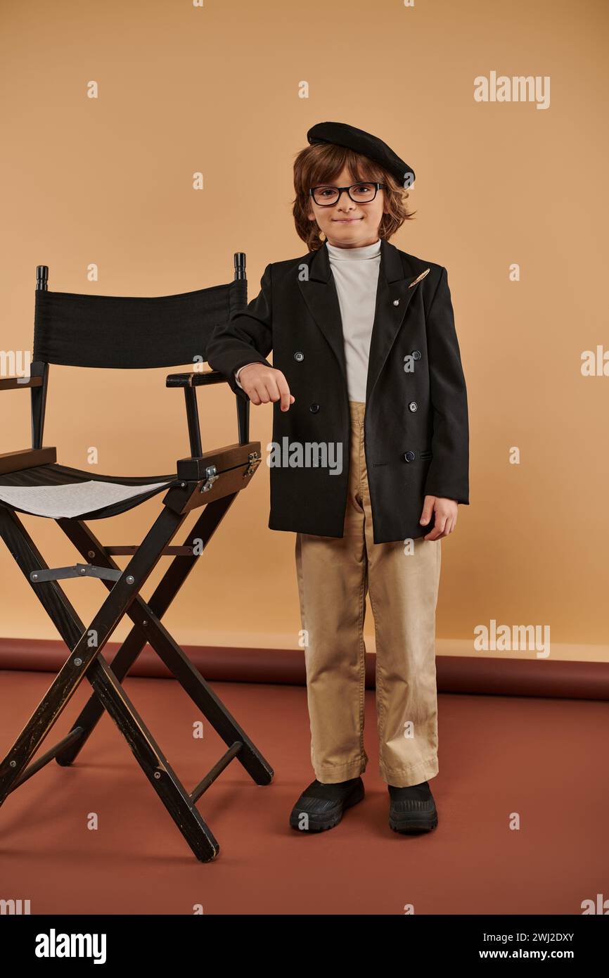 happy boy stands proudly next to director chair, wearing coat and ...