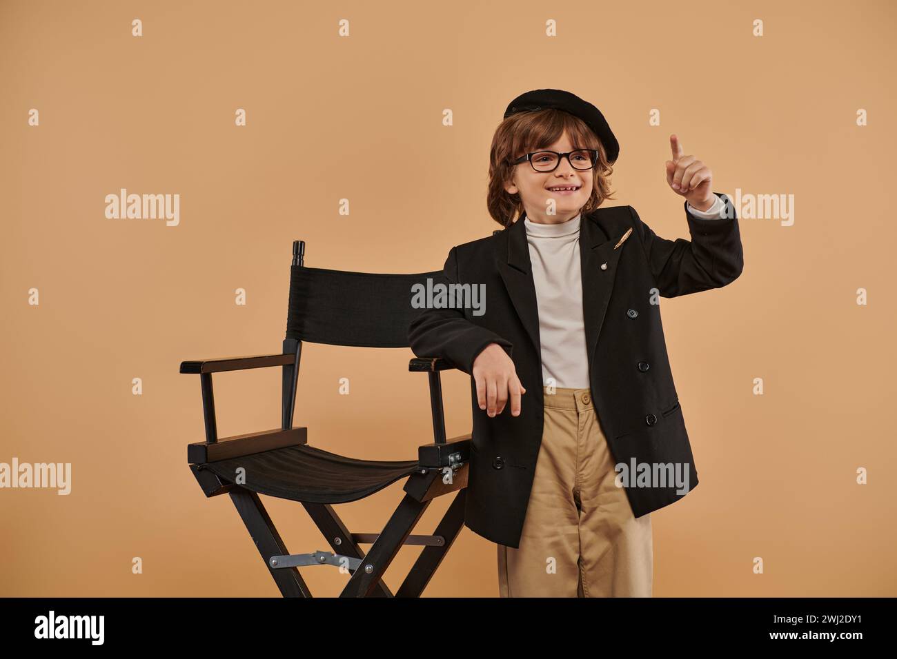 cheerful boy standing near director chair, with a smile on face showing ...
