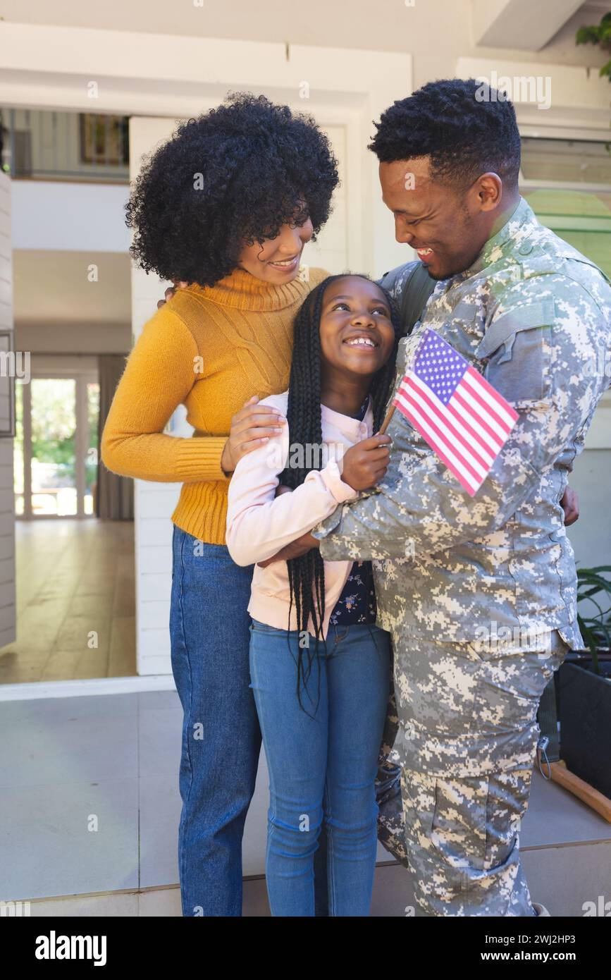 Happy african american male soldier embracing family outside home with ...