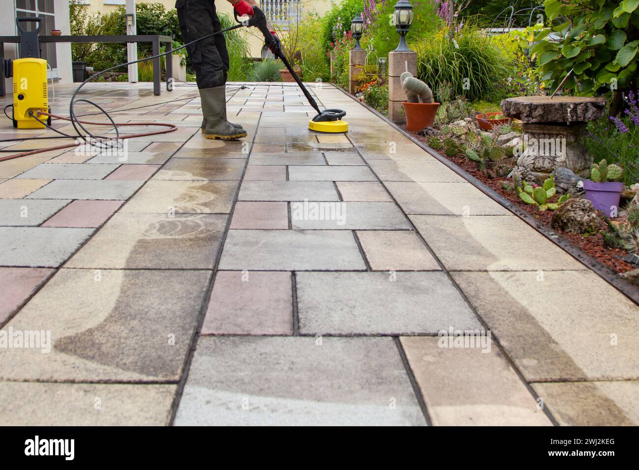 Cleaning stone slabs on patio with the high-pressure cleaner. Person ...