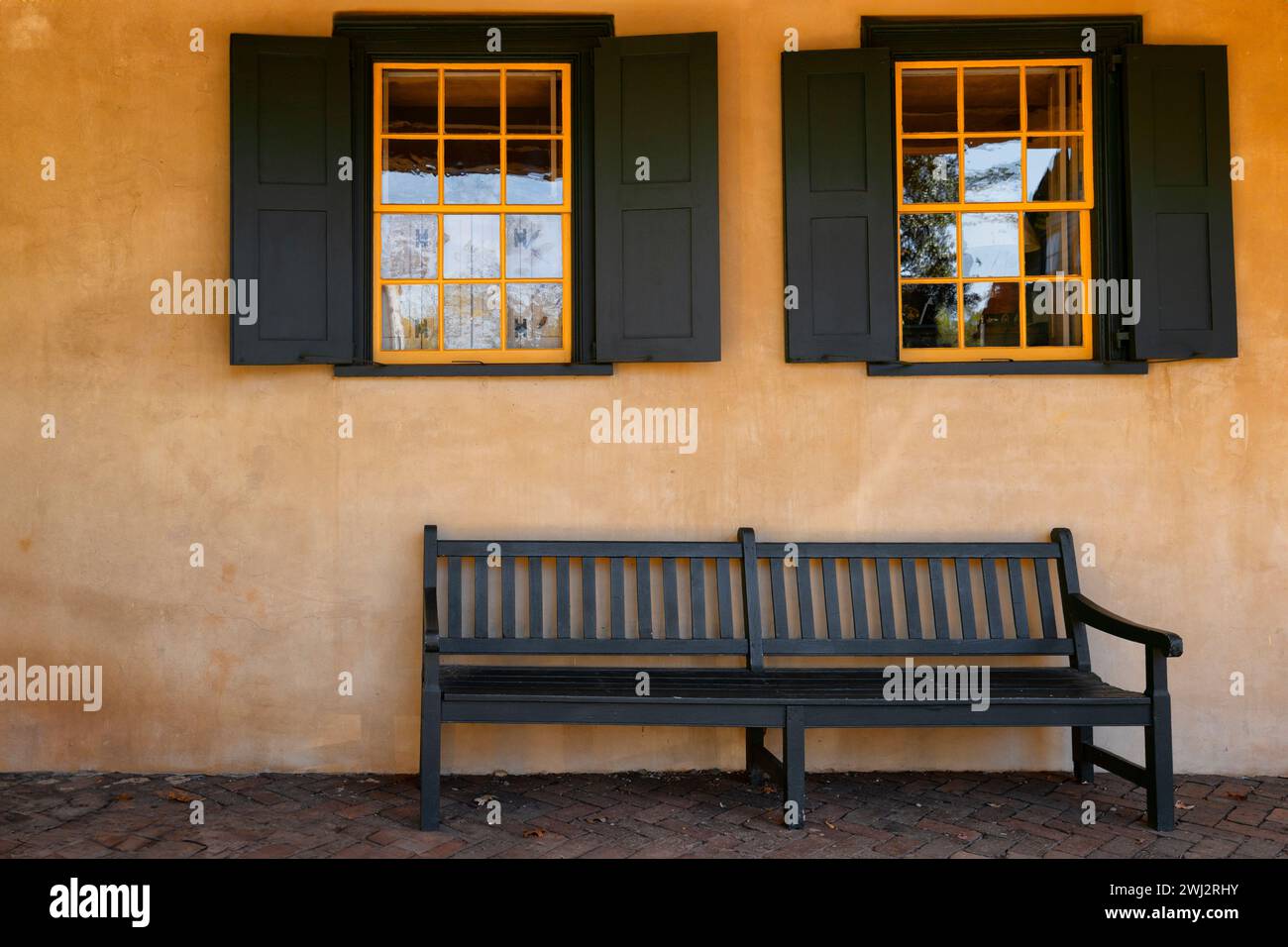 Exterior wall of a building with two windows, shutters matching bench ...