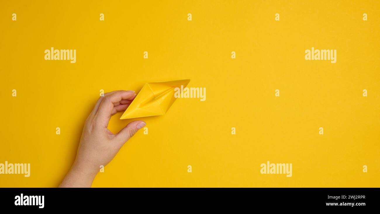 Female hand hold a blue paper boat on a yellow background. Mentoring ...