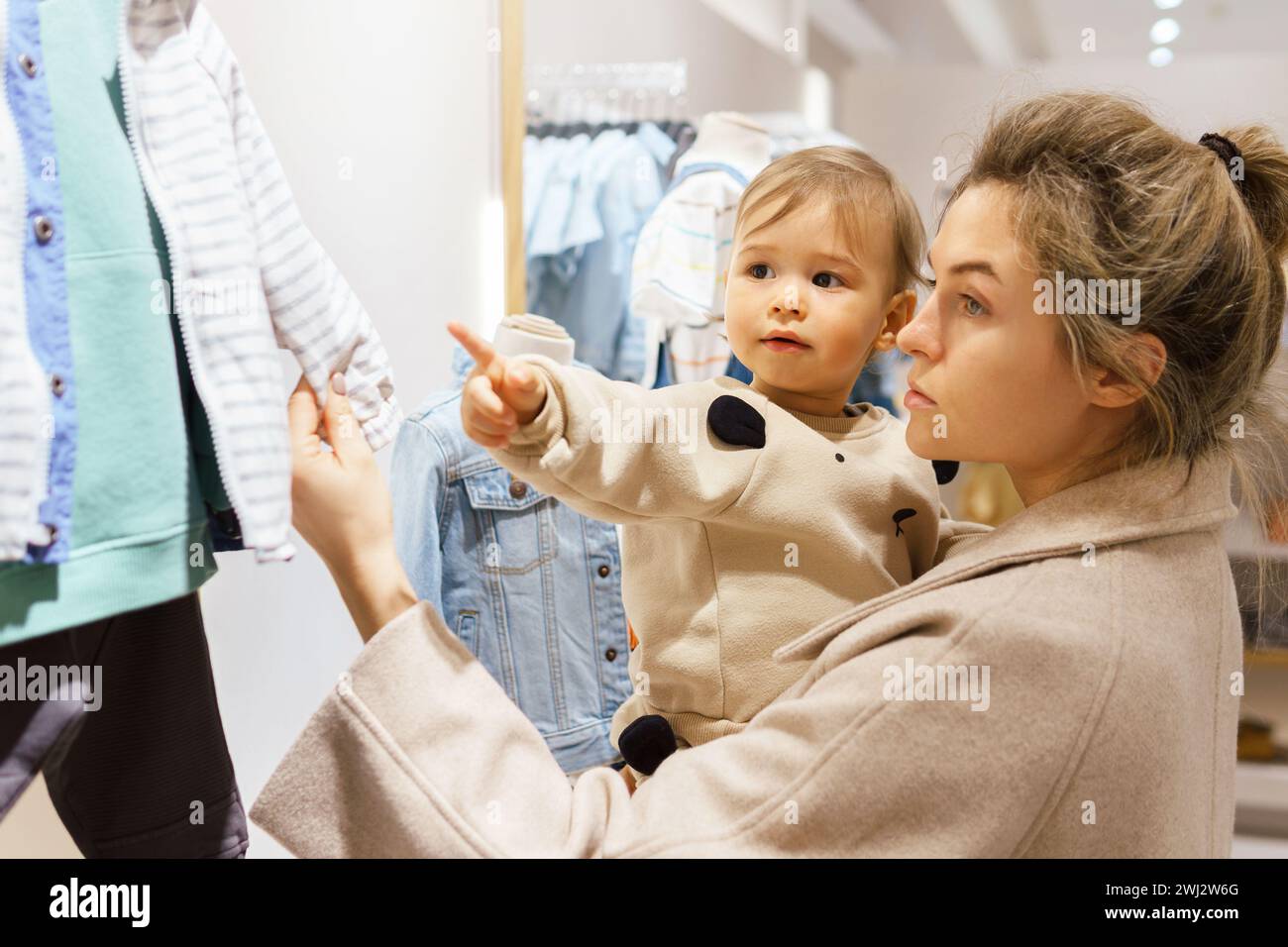 Woman with her baby son choosing clothing in clothes store Stock Photo ...