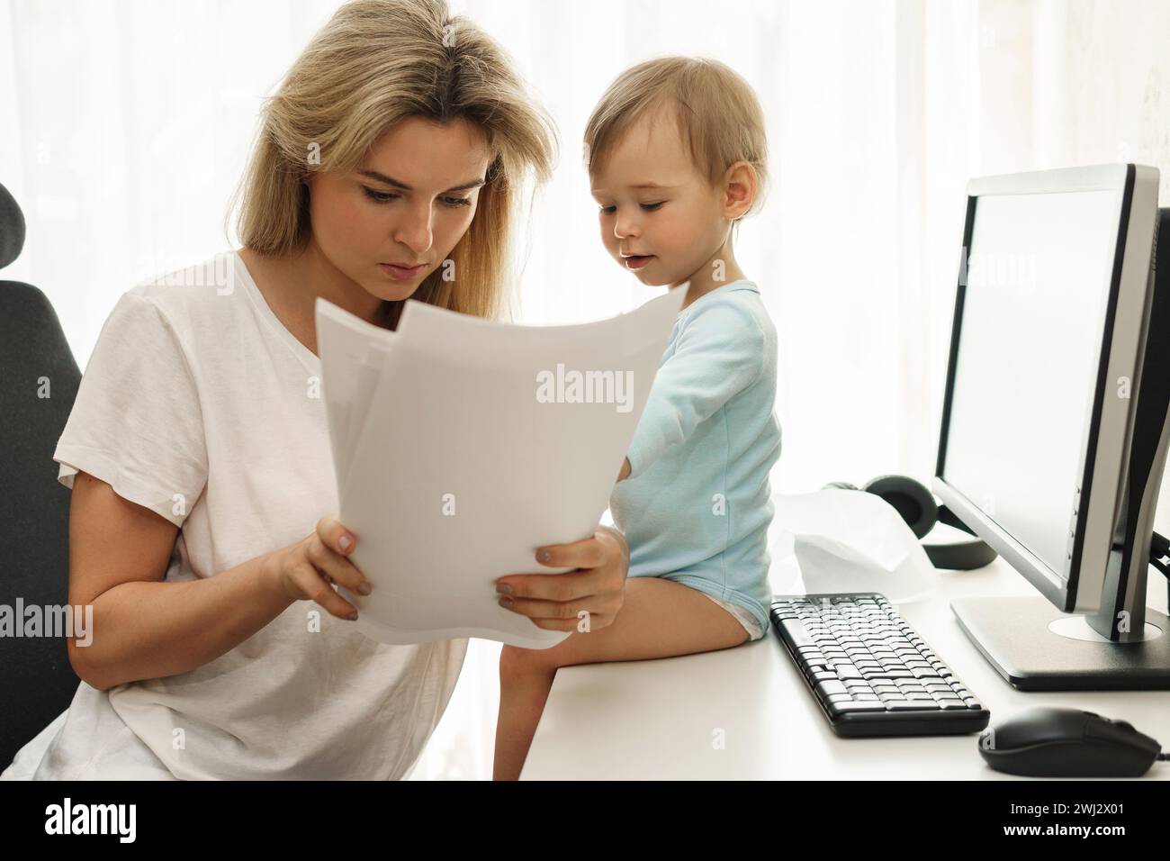 Young freelancer mother reading papers at home office with son sitting ...