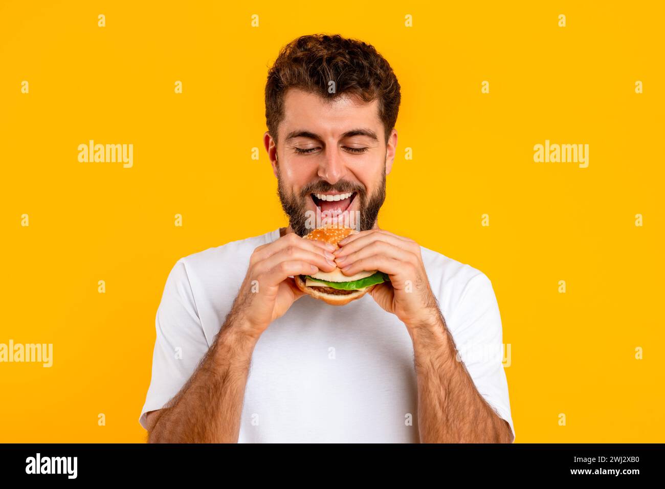 millennial guy enjoying tasty burger over yellow backdrop Stock Photo ...