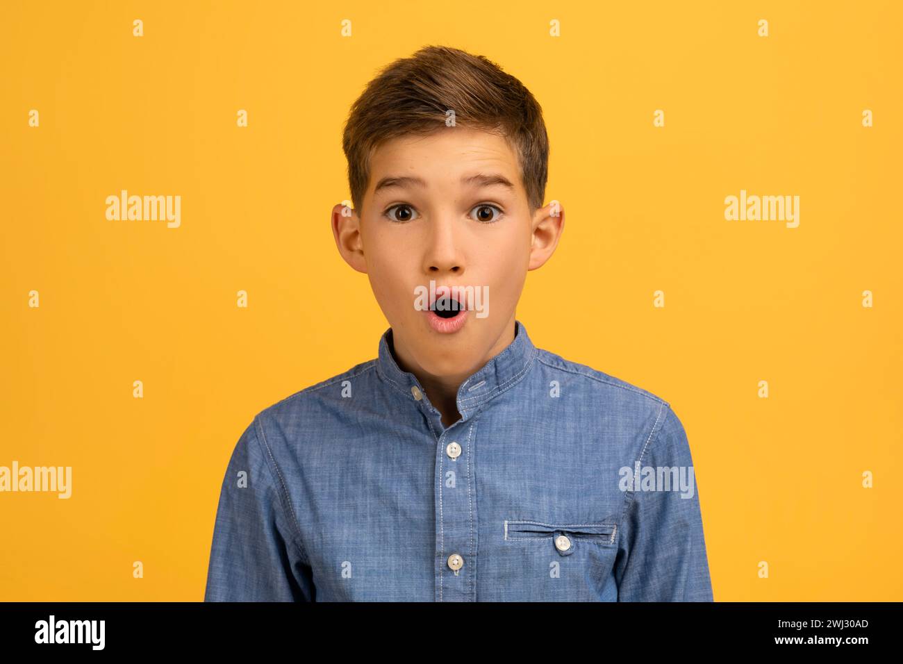 Astonished teenage boy with wide-eyed expression posing against yellow ...