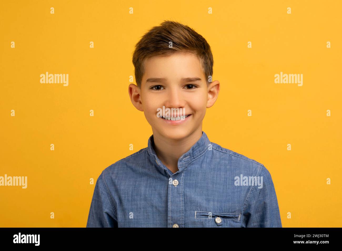 Happy teen boy with charming smile posing against vibrant yellow studio ...