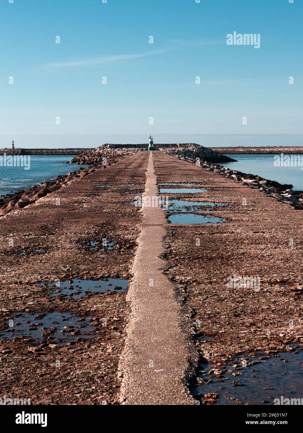 A bumpy pedestrian road with puddles along a breakwater, flanked by the ...