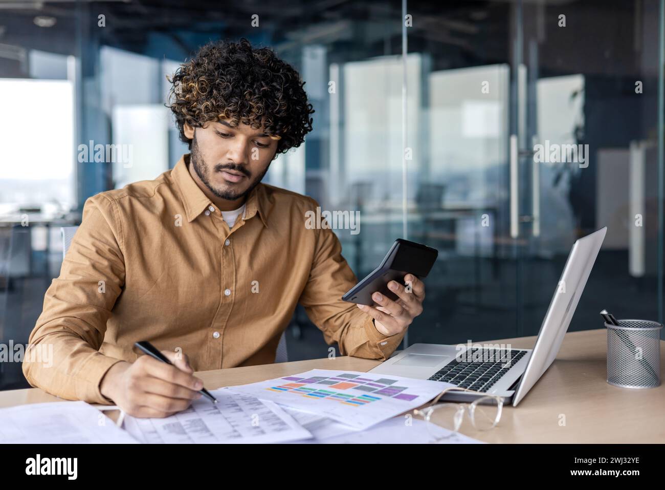 Serious and focused young Indian man working in office at desk with ...