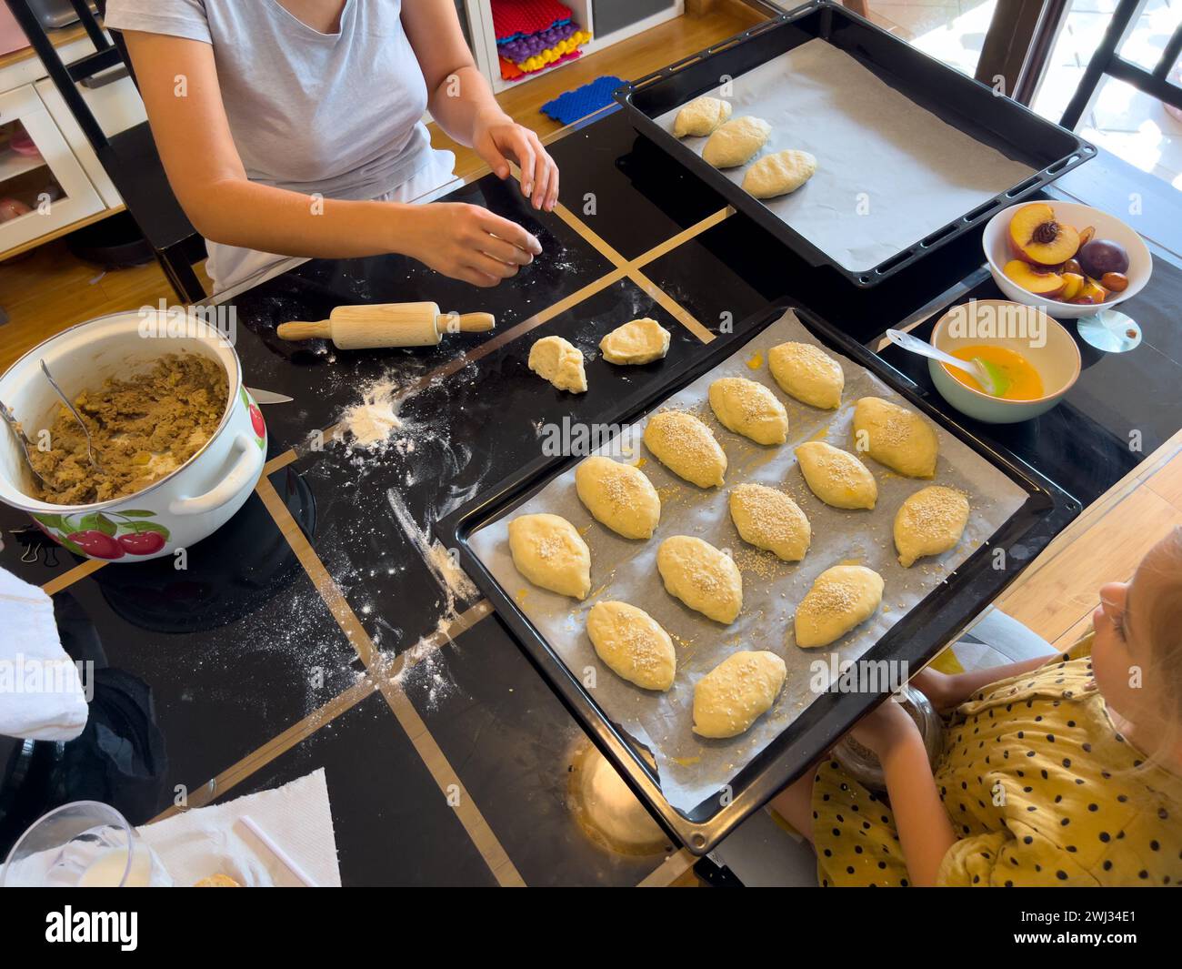 Little girl looks at her mother making buns at the table. High quality ...