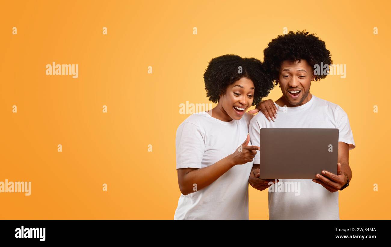 African american couple using laptop together, colorful studio ...