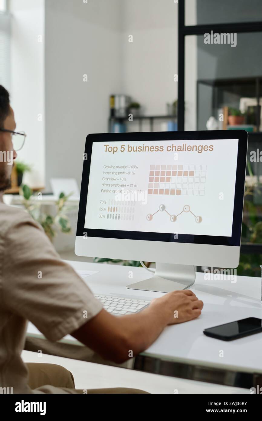 Young modern analyst sitting by desk in front of computer monitor with ...