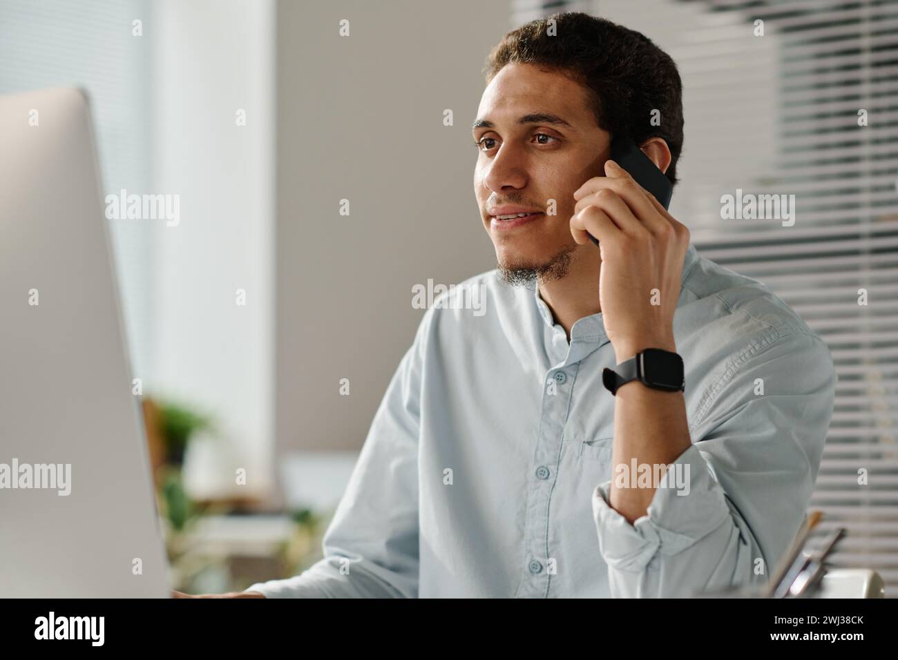 Young male employee talking to someone by mobile phone while sitting in ...