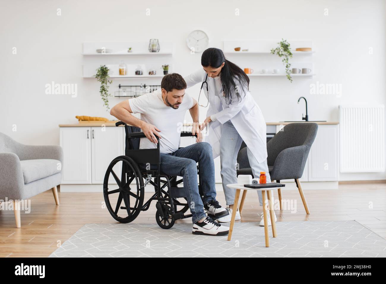 Female in doctor's coat supporting bearded male rising from wheelchair ...