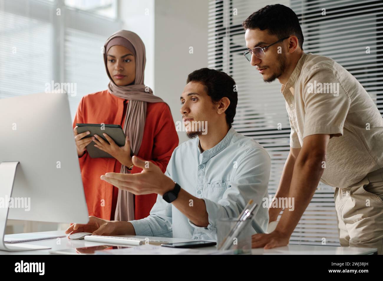Team of three young Muslim employees looking at computer screen while ...