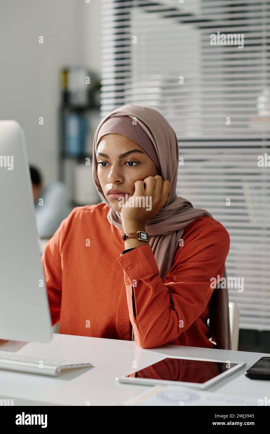 Young bored businesswoman in hijab sitting in front of desktop computer ...