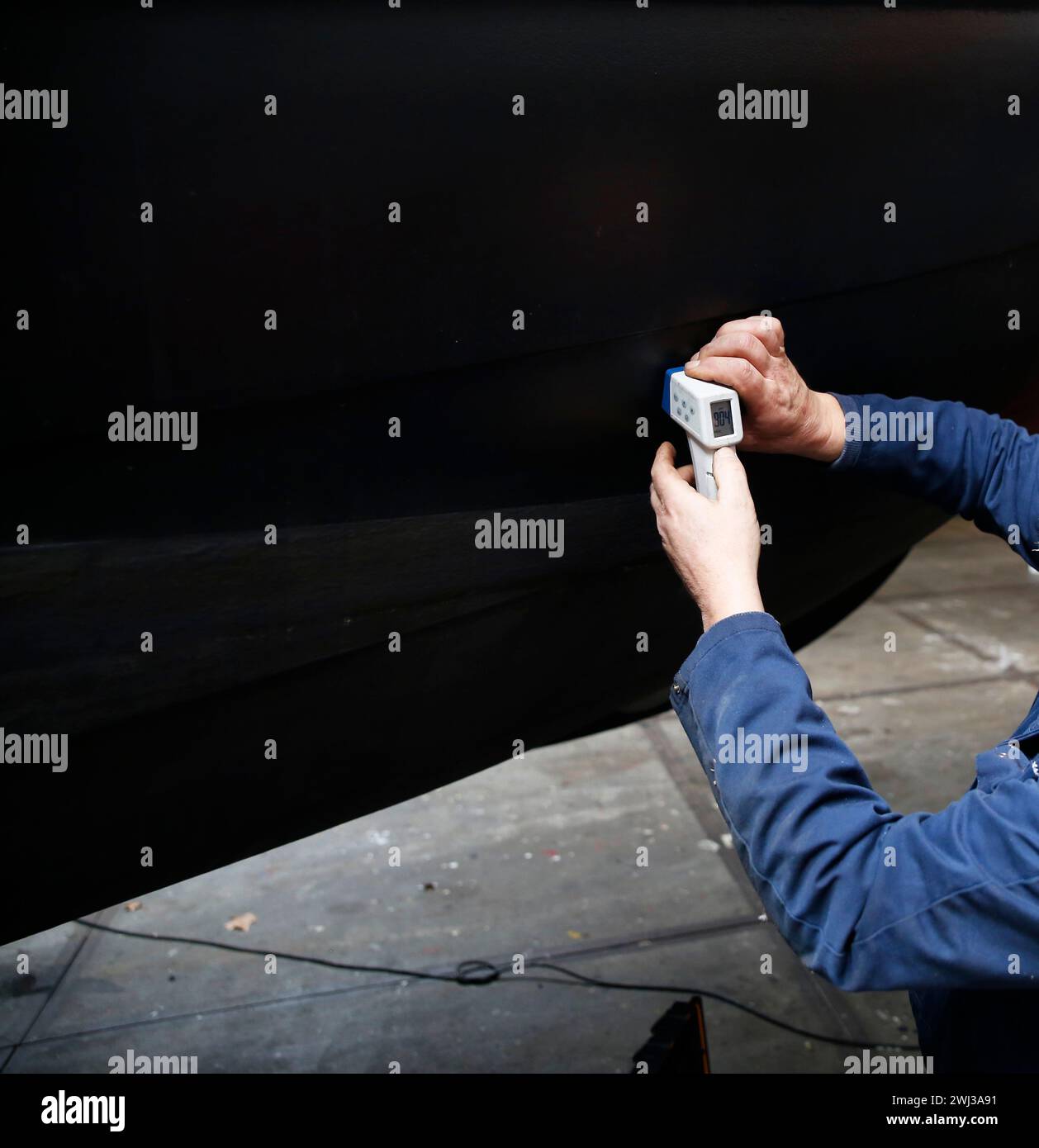 A service engineer measuring the thickness of the steel hull of a boat ...
