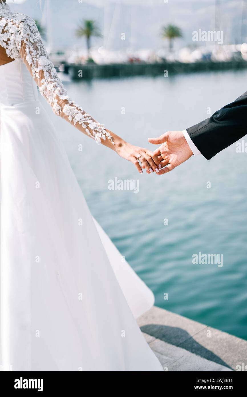 Bride hand touches the palm of groom standing on the pier. Cropped ...