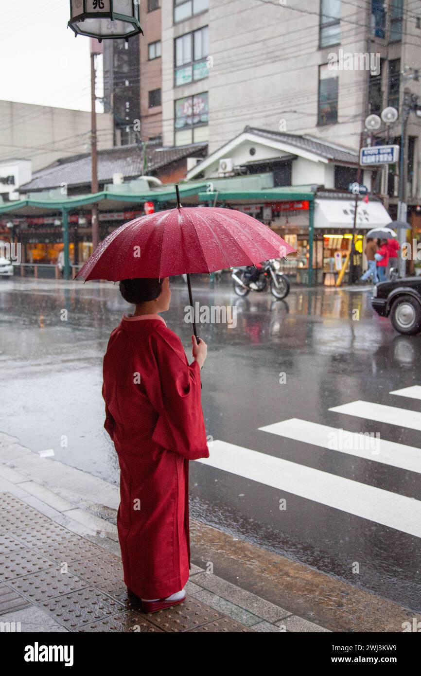 Women dressed in red kimono and red umbrella waiting to cross Shijo ...