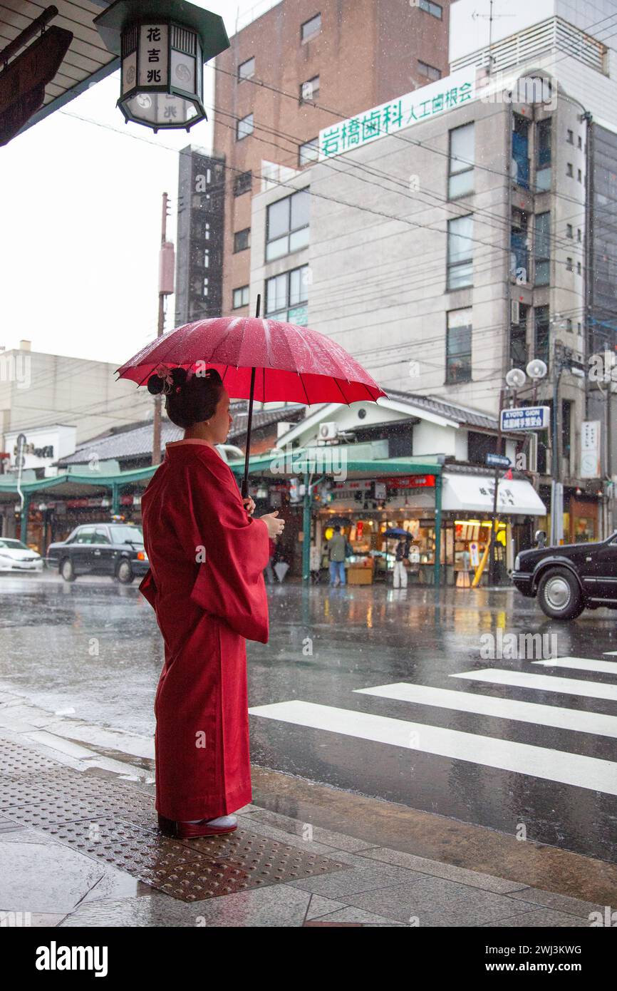 Women dressed in red kimono and red umbrella waiting to cross Shijo ...