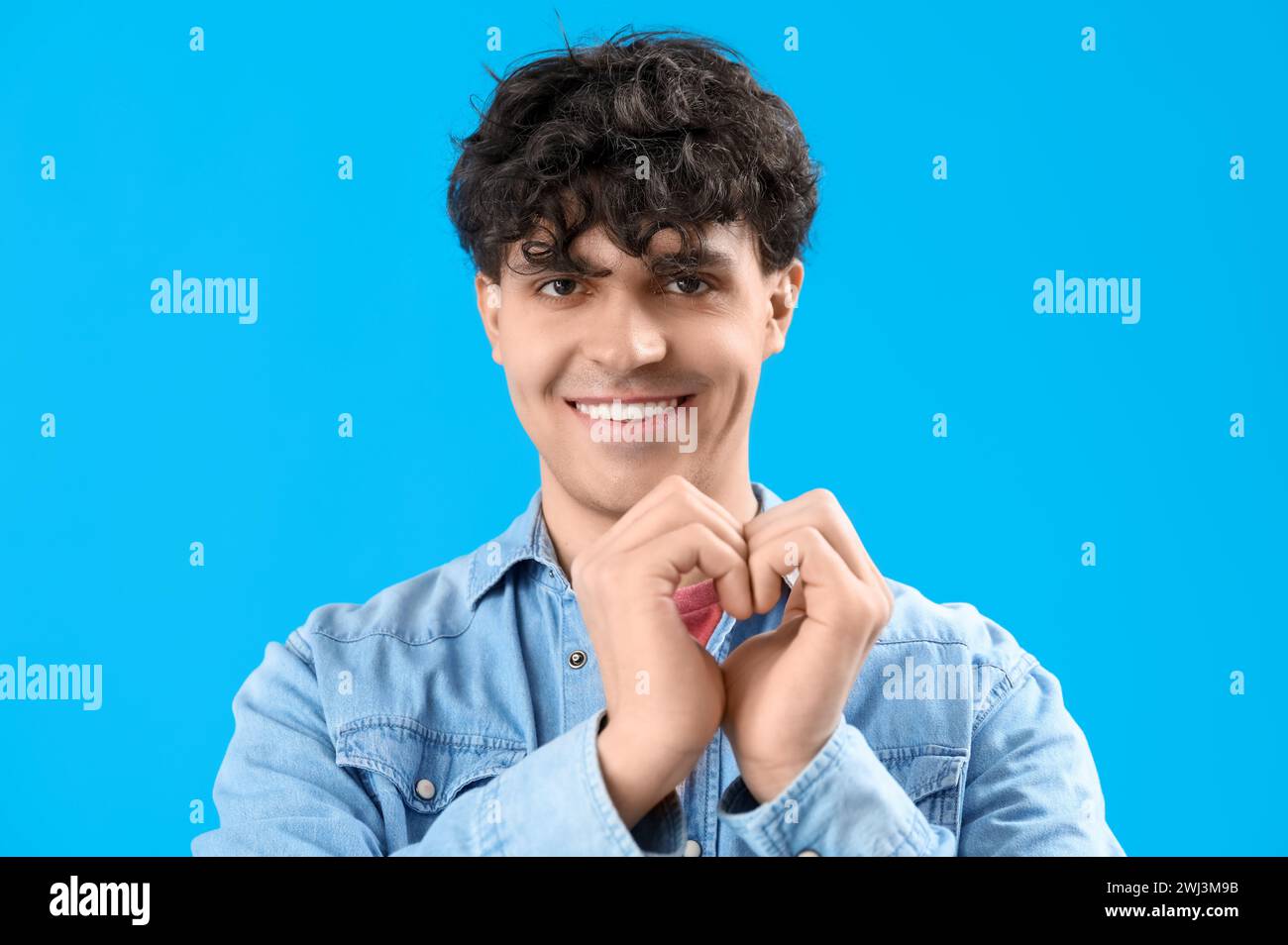 Handsome young man making heart with his hands on light blue background ...