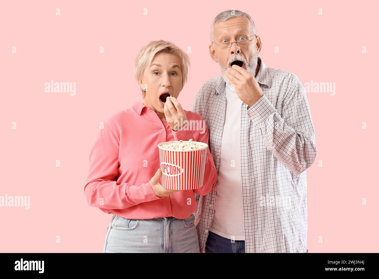 Shocked mature couple eating popcorn on pink background Stock Photo - Alamy