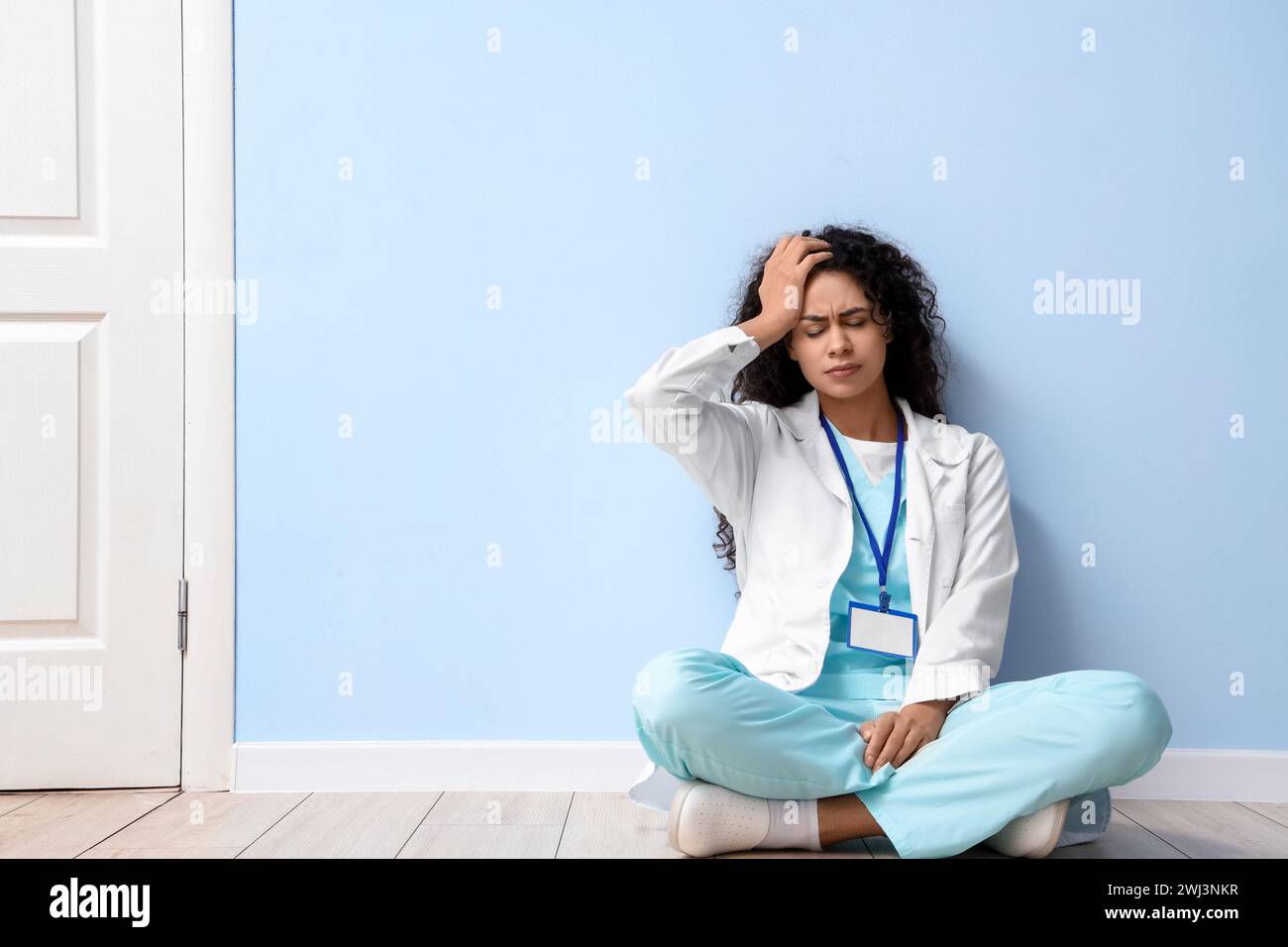 stressed female African-American medical intern sitting near blue wall ...