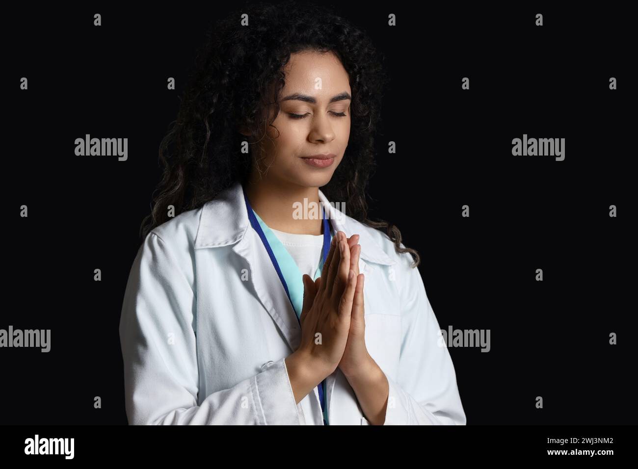 Female African-American medical intern praying on black background ...