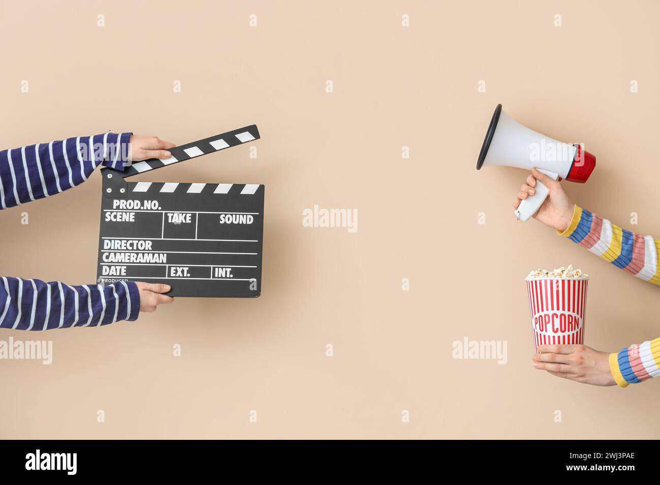 Hands with movie clapper, bucket of popcorn and megaphone on beige ...