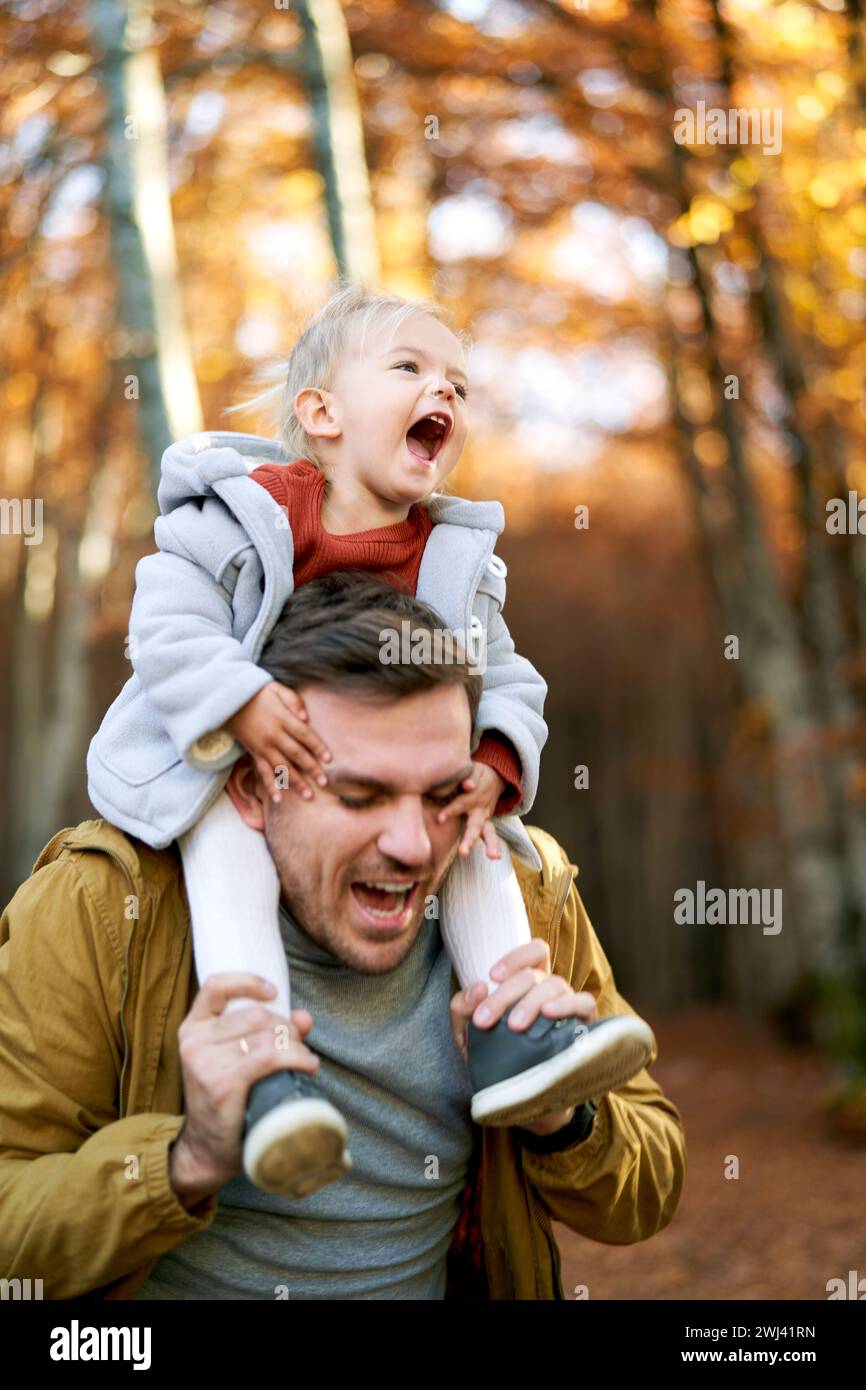 Little laughing girl sits on the shoulders of a laughing dad. Portrait ...