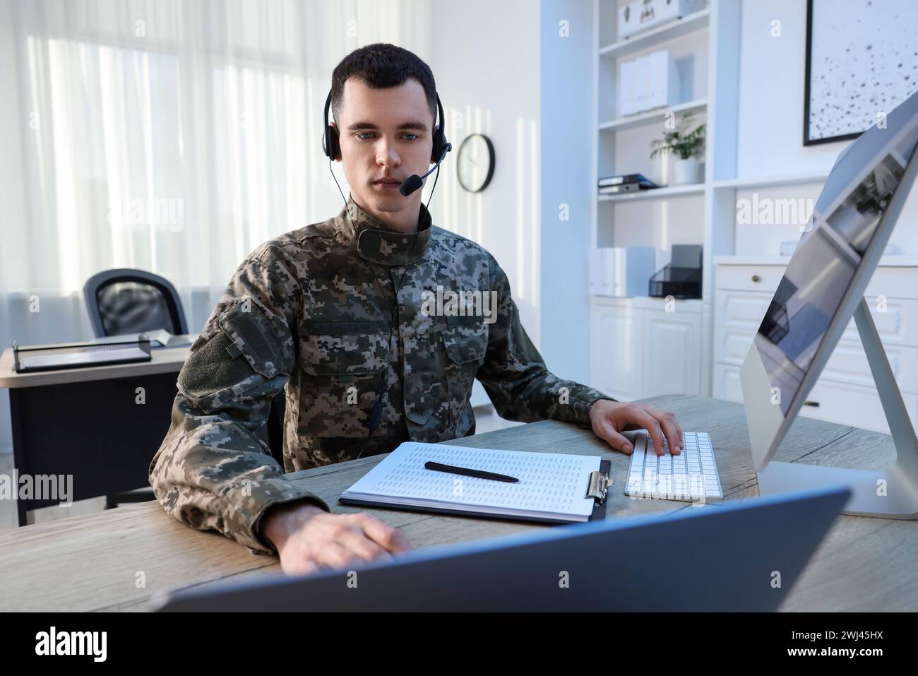 Military service. Young soldier in headphones working at wooden table ...
