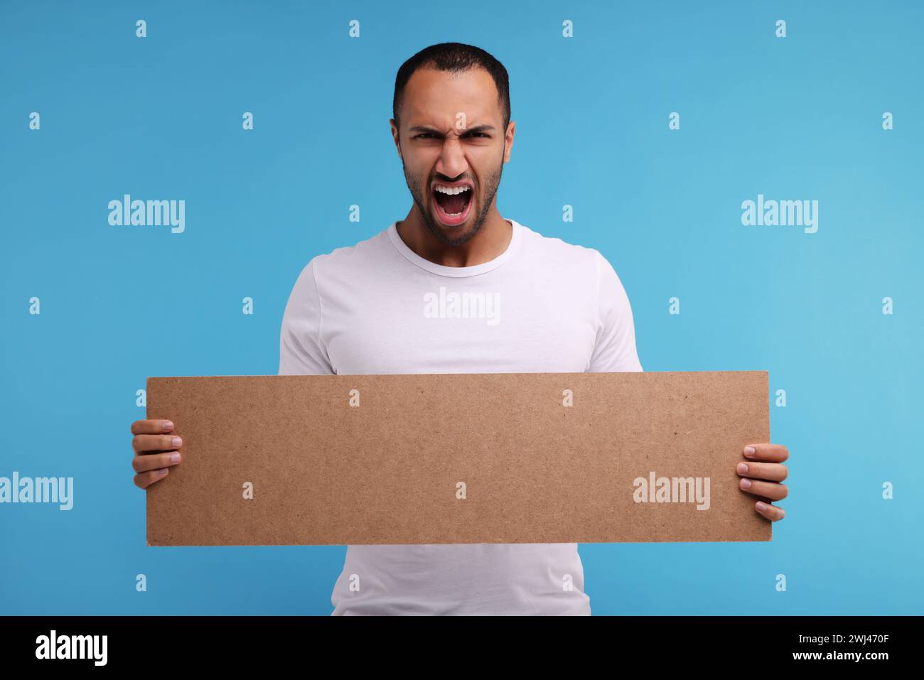 Angry man holding blank cardboard banner on light blue background ...