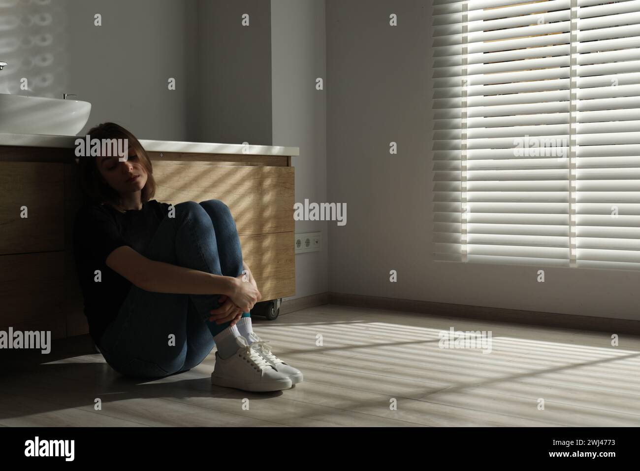 Sad young woman sitting on floor in bathroom, space for text Stock ...