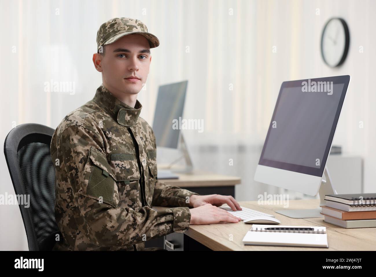 Military service. Young soldier working with computer at wooden table ...