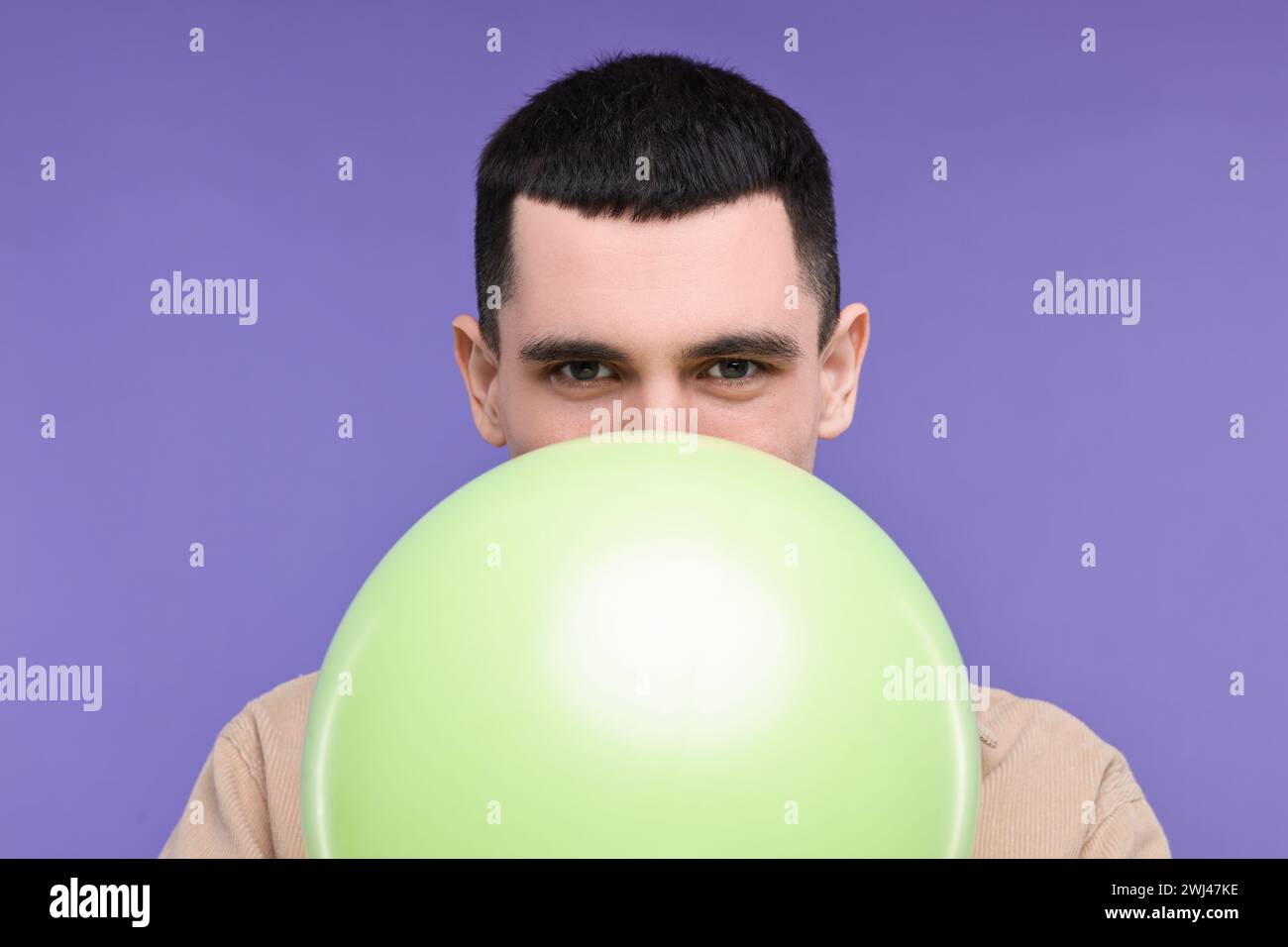 Young man inflating light green balloon on purple background Stock ...