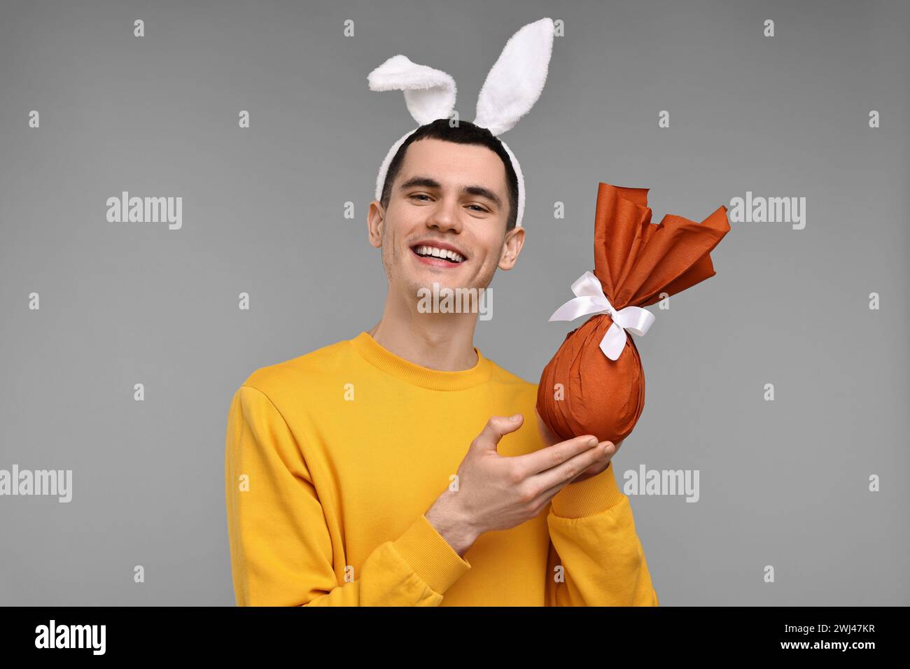 Easter celebration. Handsome young man with bunny ears holding wrapped ...