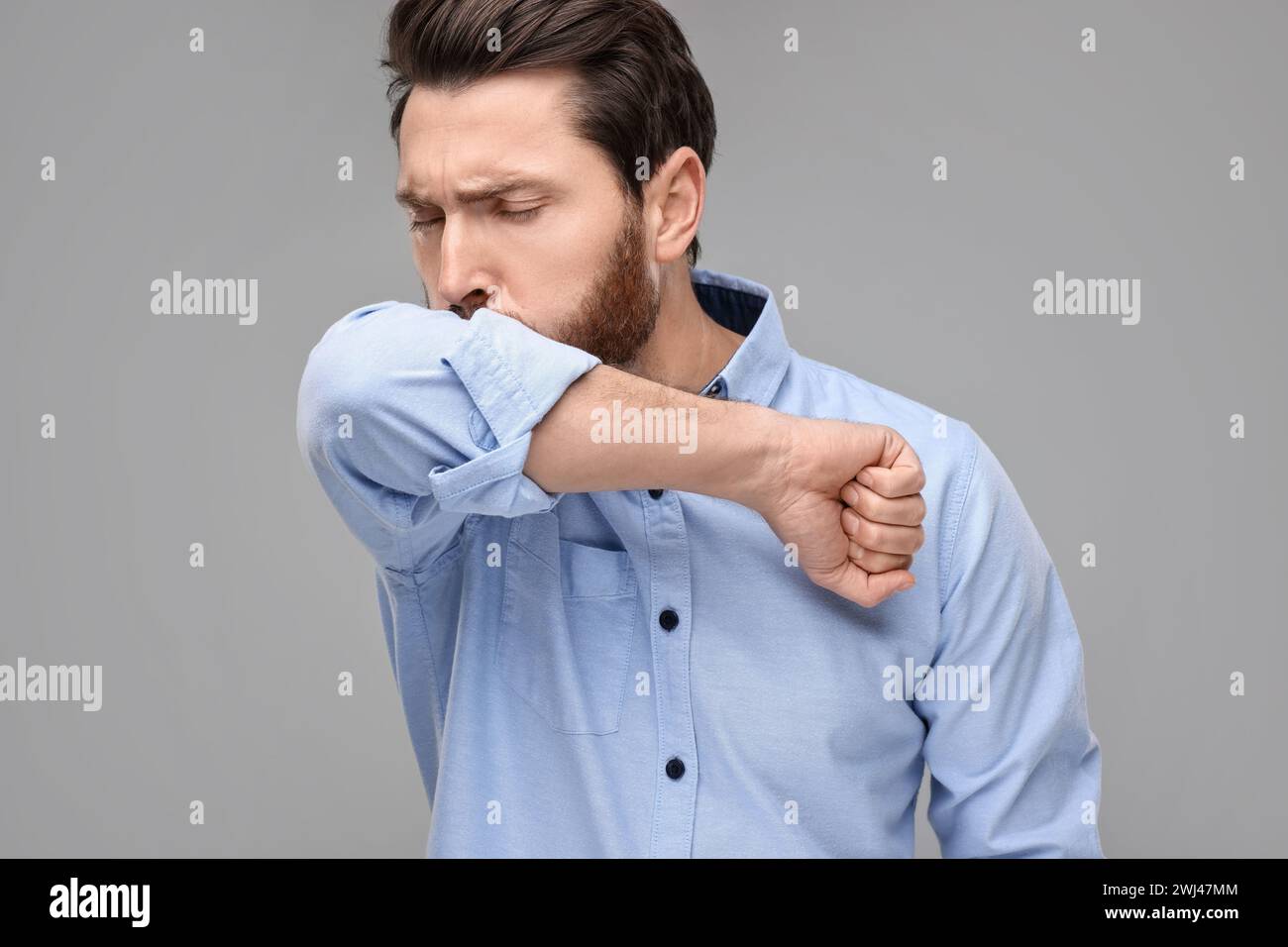 Sick man coughing into his elbow on light grey background. Cold ...