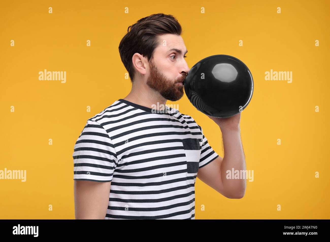 Man inflating black balloon on yellow background Stock Photo - Alamy