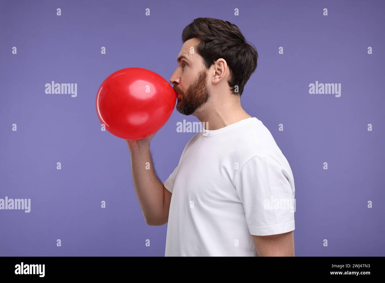 Man inflating red balloon on purple background Stock Photo - Alamy