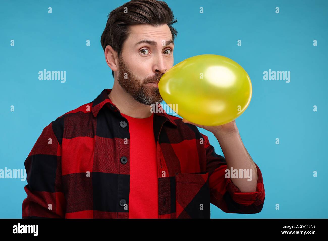Man inflating yellow balloon on light blue background Stock Photo - Alamy