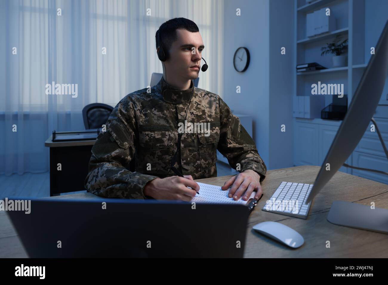 Military service. Young soldier in headphones working at wooden table ...