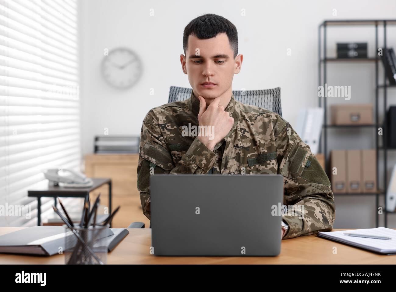 Military service. Young soldier working with laptop at table in office ...