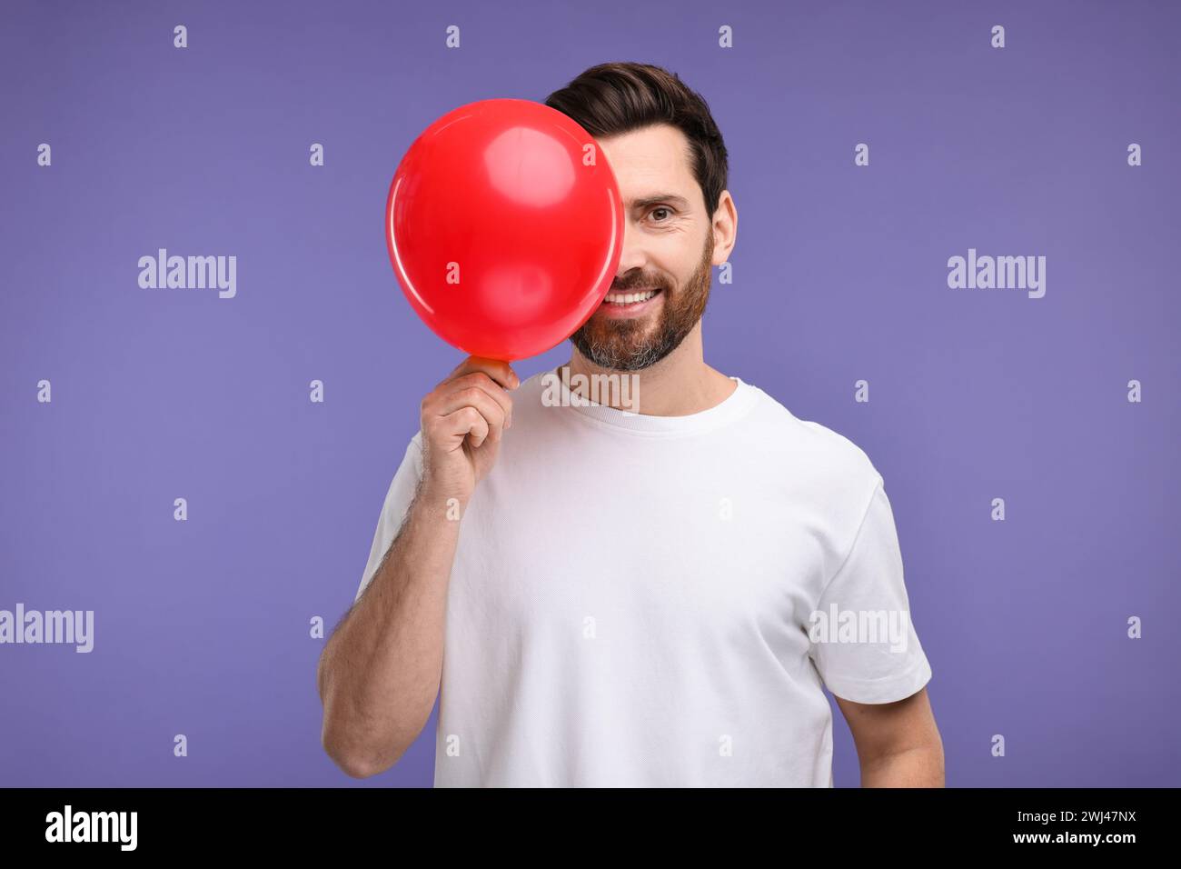 Man inflating red balloon on purple background Stock Photo - Alamy