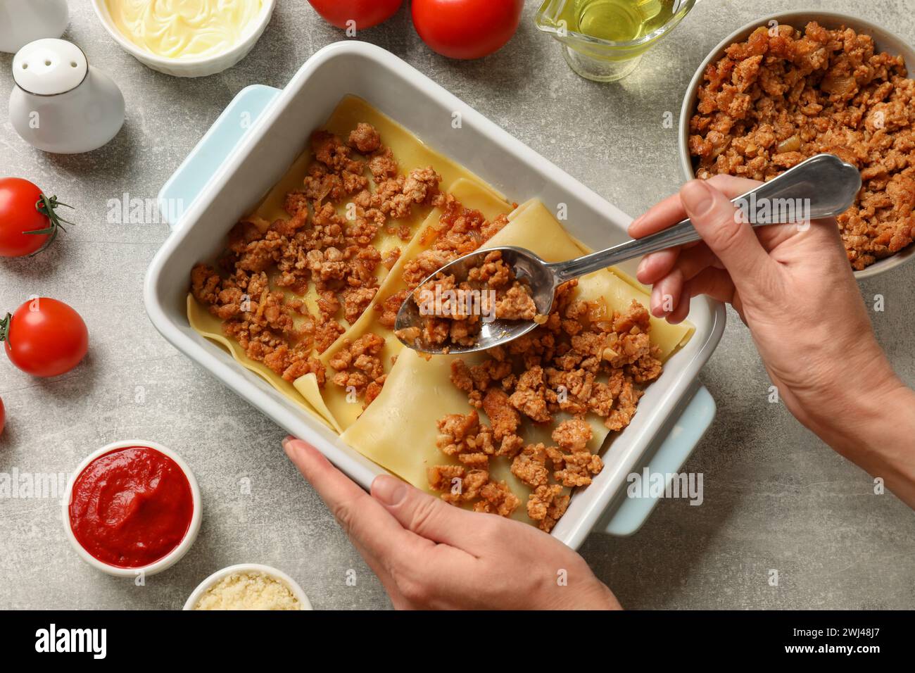 Woman making lasagna at light grey textured table, top view Stock Photo ...