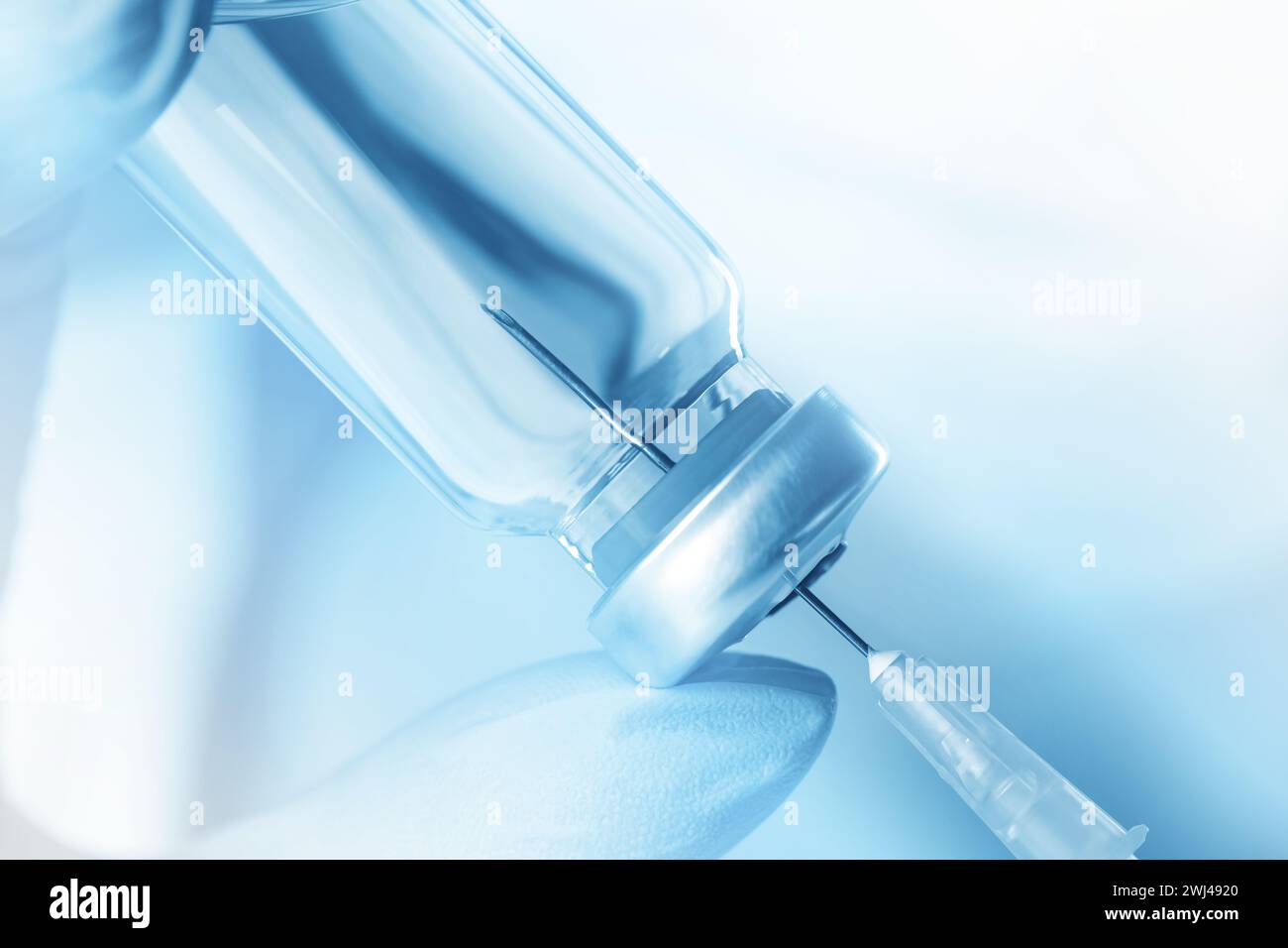 Doctor filling syringe with medication from vial, toned in light blue ...
