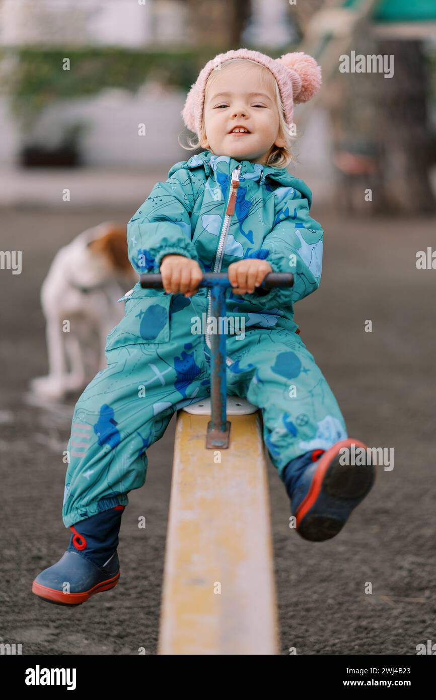 Smiling little girl swings on a swing-balancer, holding the handle and ...