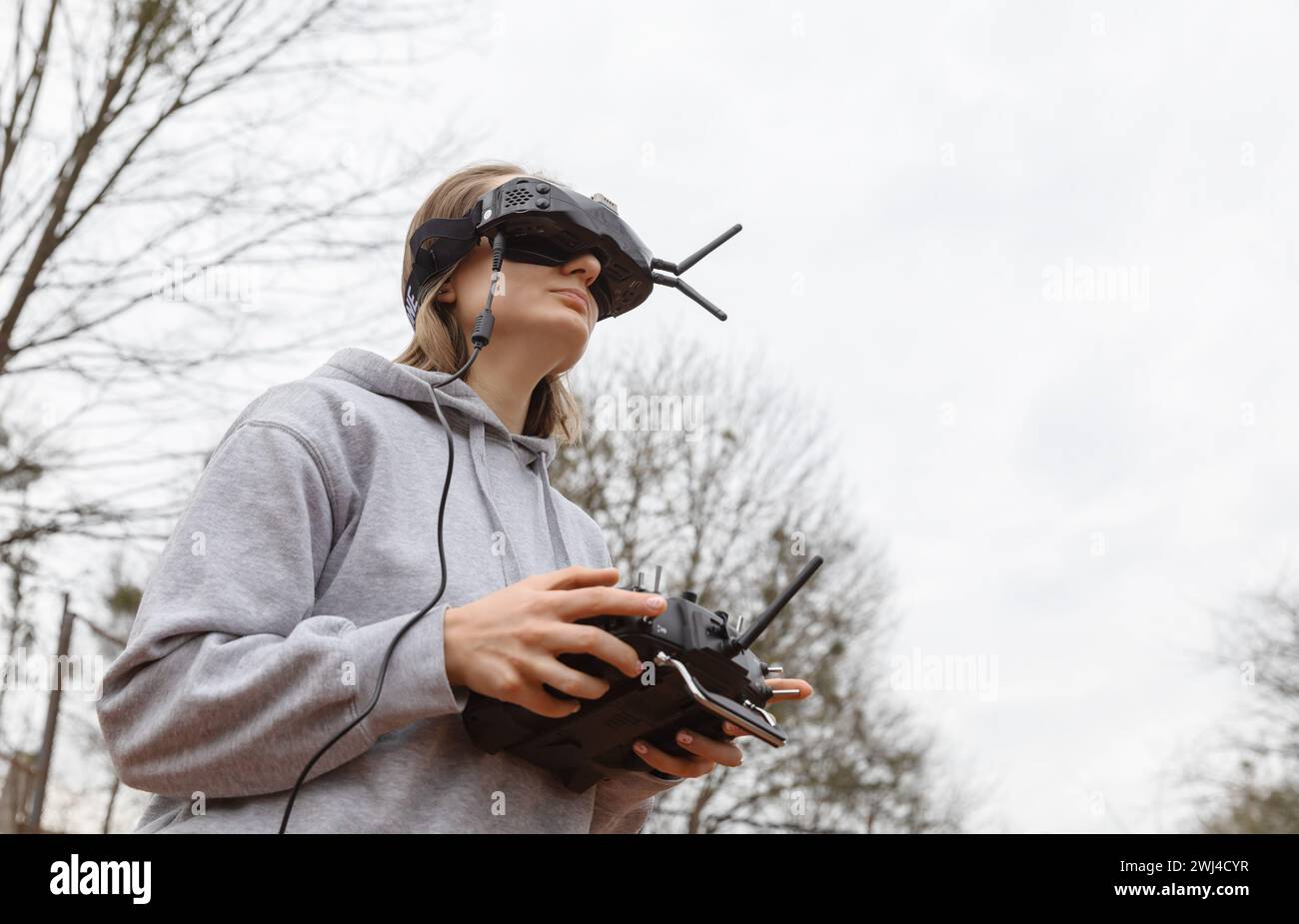 A young woman wears virtual reality goggles and holds a remote control ...